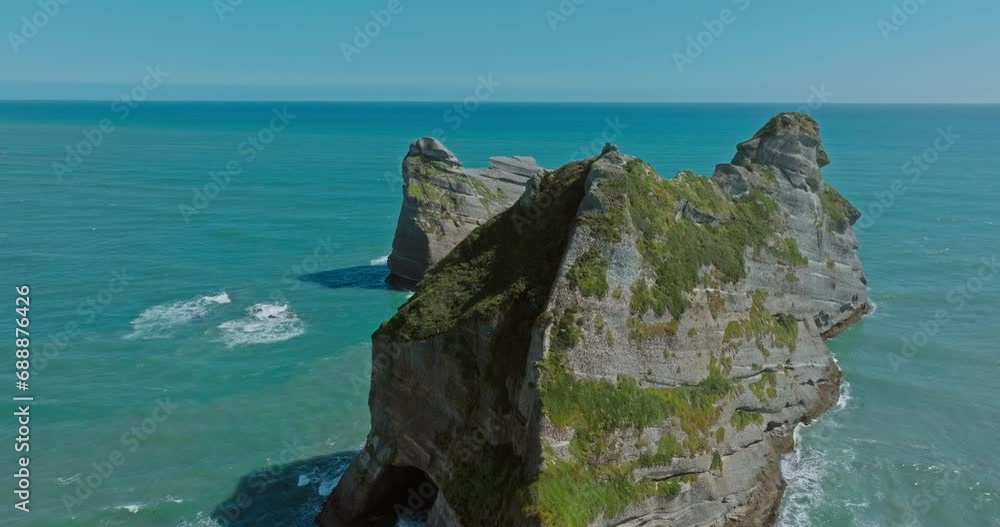 Aerial flight over wild, rugged rock formation with arch in the Tasman ...