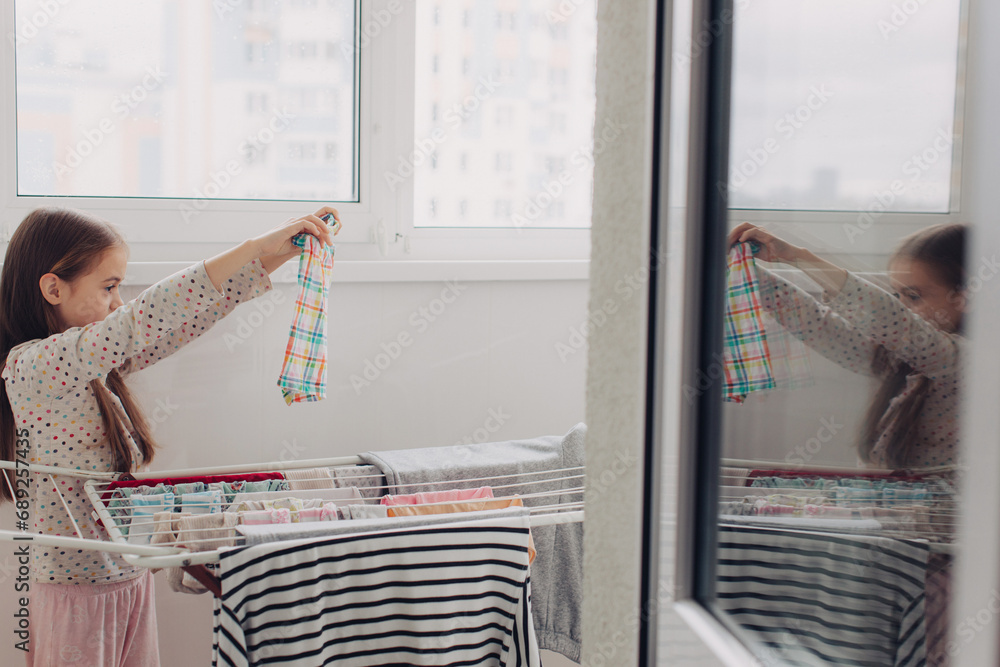 Teen girl in laundry room. Clean washed clothes on drying rack. Mother ...