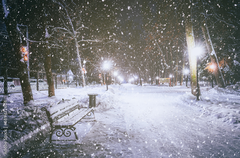 Snowfall in a winter park at night with glowing lanterns, pavement ...