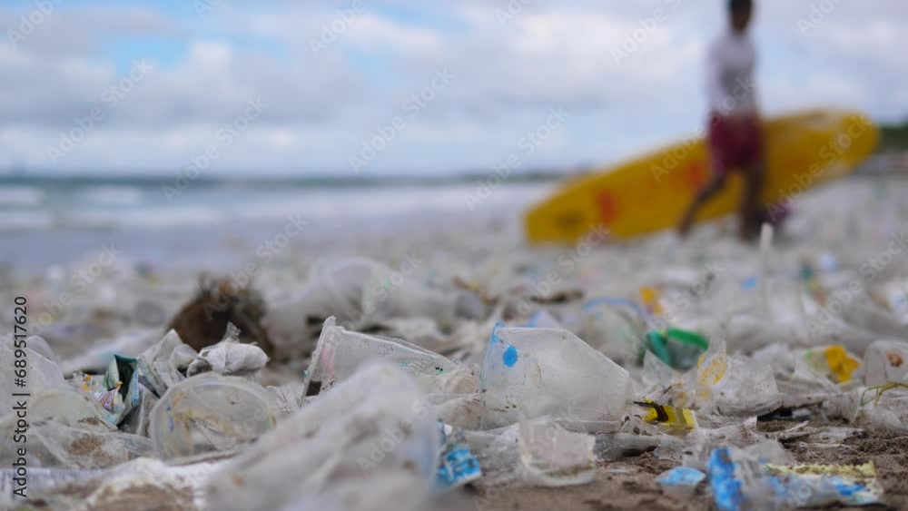 Plastic pollution on beach and man with surfboard in background. Close ...