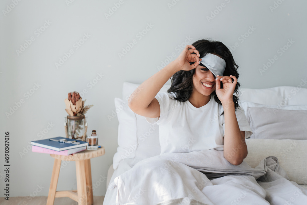 Playful young African American woman sitting on bed at morning takes ...