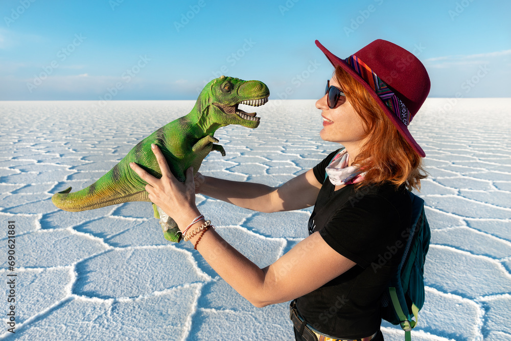A red-haired girl in a hat holds a dinosaur in her hands and looks at ...