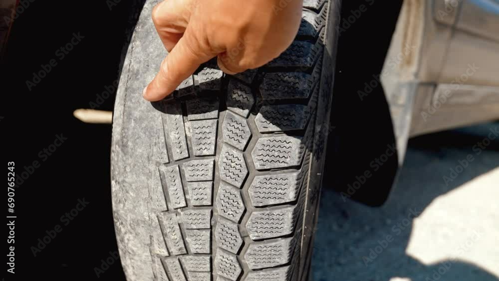 Finger of man's hand pointing at old, damaged and worn black tire tread ...