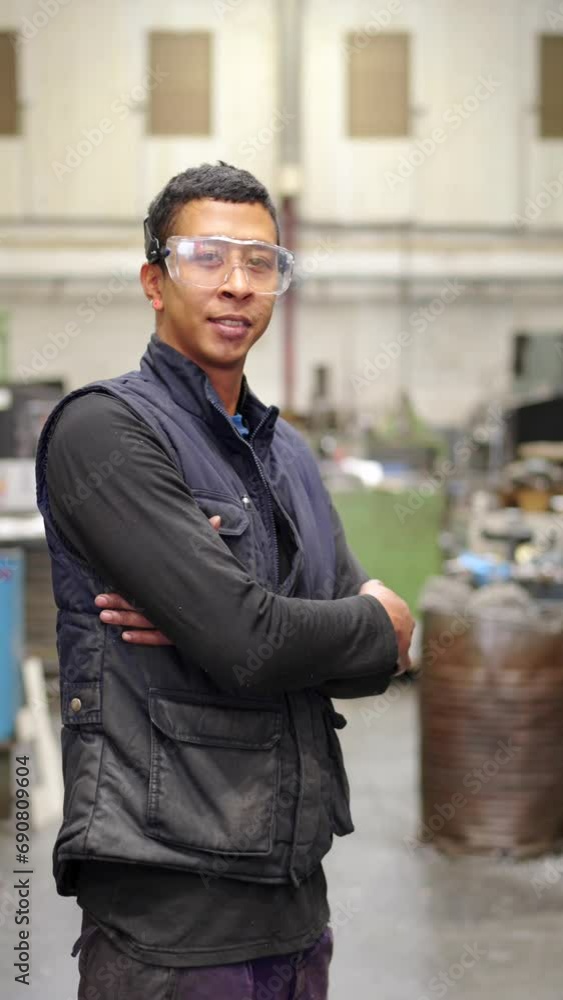 Vertical video zooming out of a proud worker of a factory standing ...