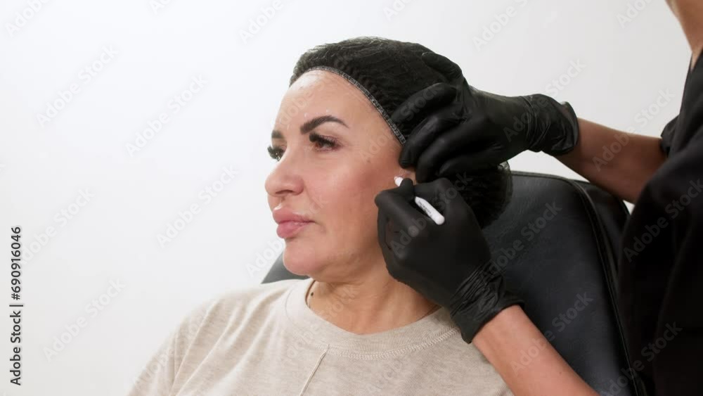 A female cosmetologist makes marks on her face for injections in a ...