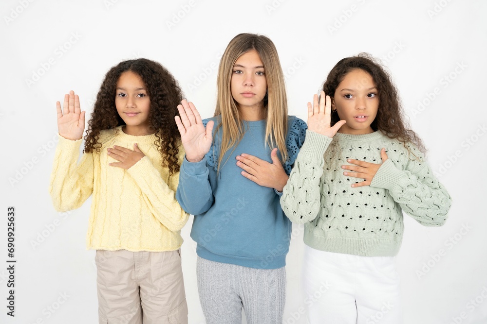 Three beautiful multiracial kid girls Swearing with hand on chest and ...