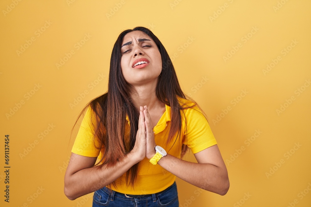 Young arab woman standing over yellow background begging and praying ...