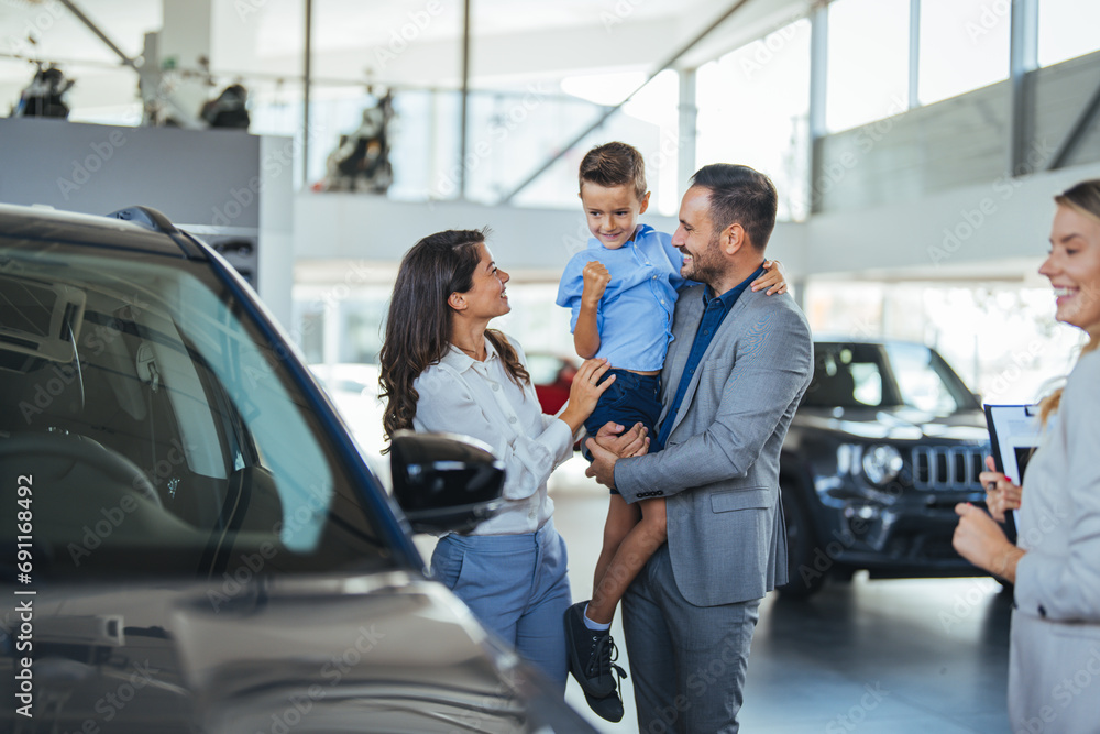 Young happy family enjoying while buying a new car in a showroom ...