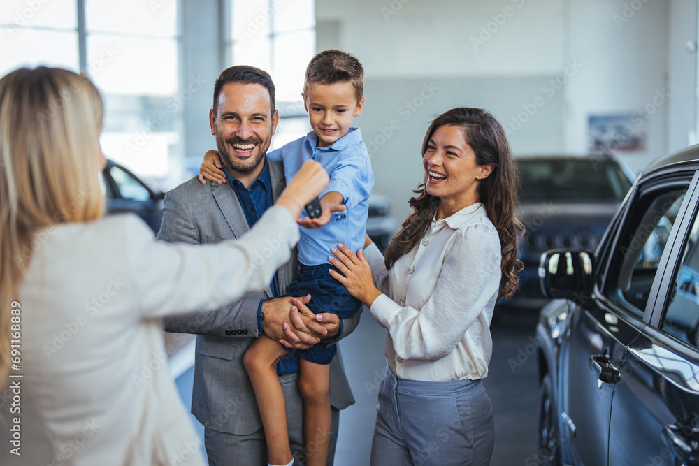 Happy family holding the keys of their new car at the dealership ...