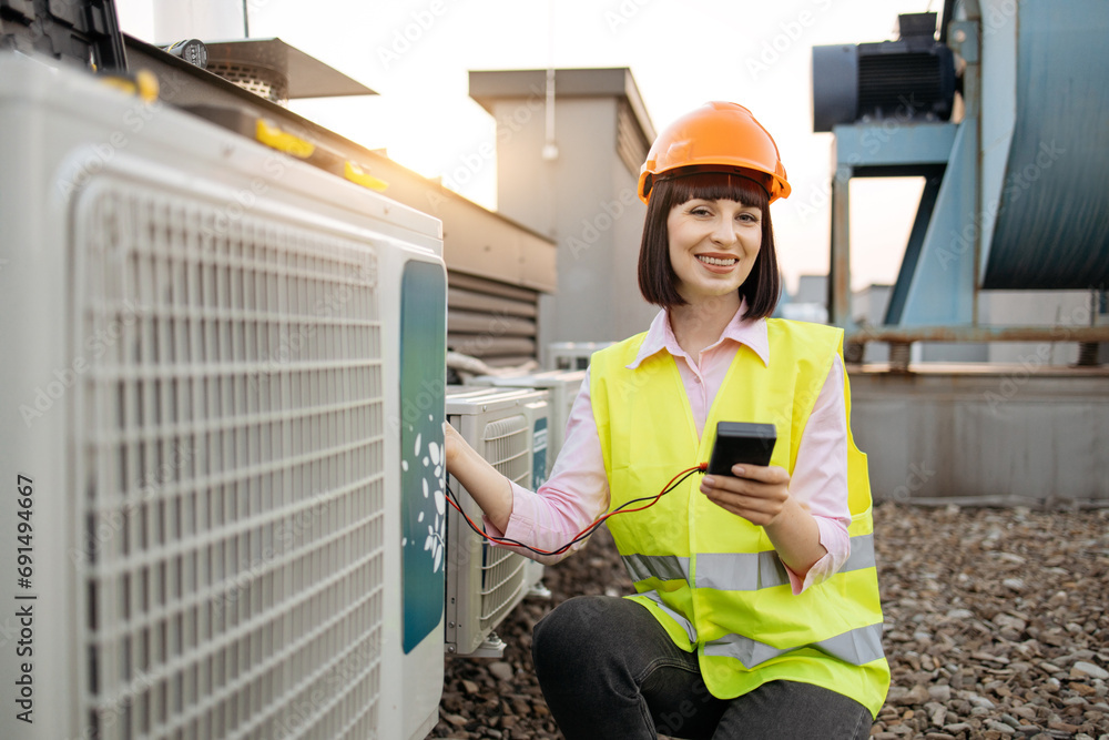 Beautiful repairwoman kneeling in front of air conditioner while ...