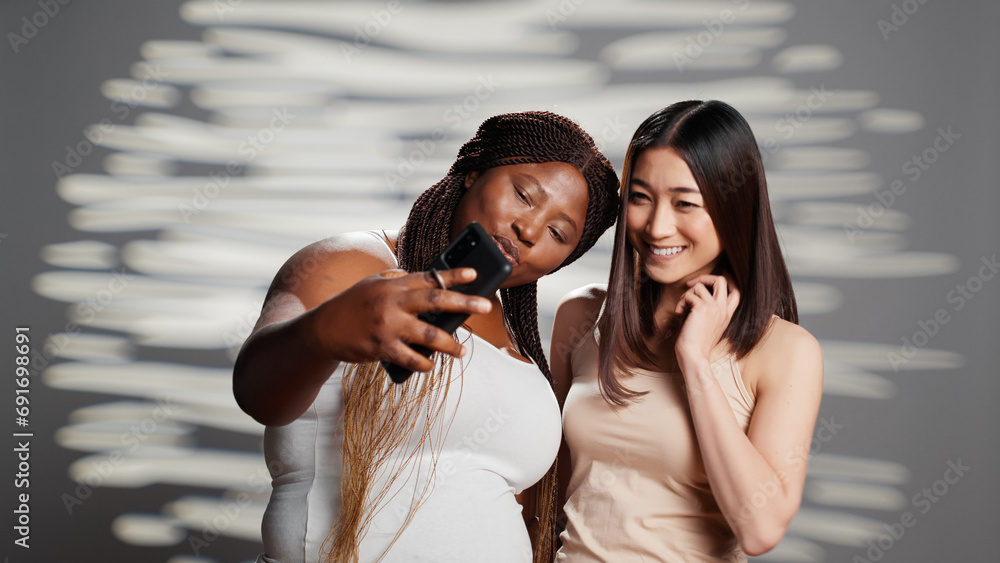 Two skincare models taking photos with smartphone, diverse young women ...