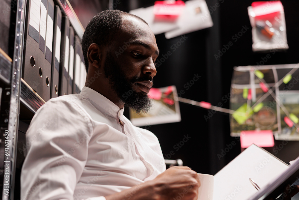 African american investigator reading police documentation, working late. Man detective studying ...