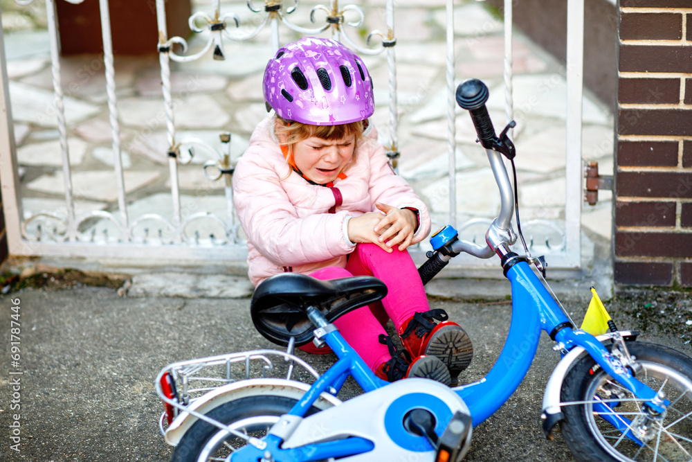 Cute little girl sitting on the ground after falling off her bike ...
