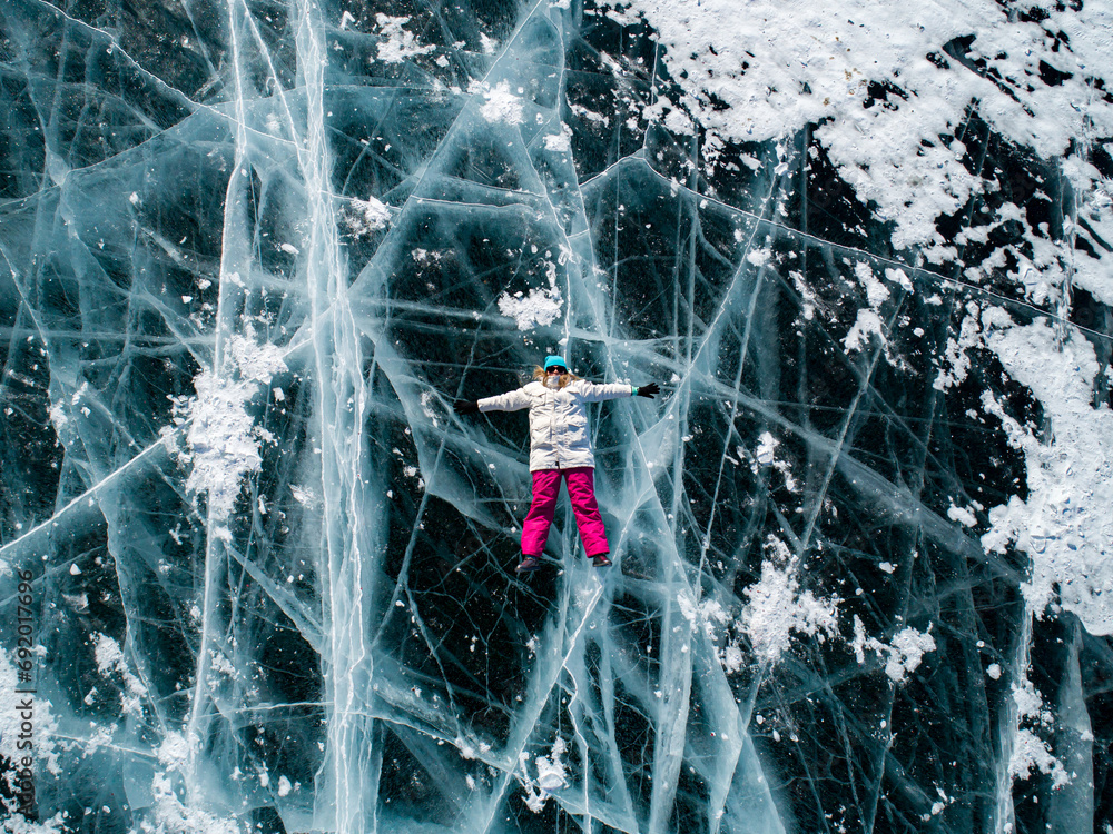 Aerial top down shot of the young woman lying on the blue cracked ice ...