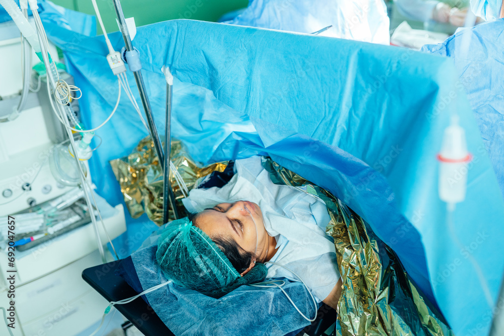 A young woman on surgery table during complex surgical operation ...