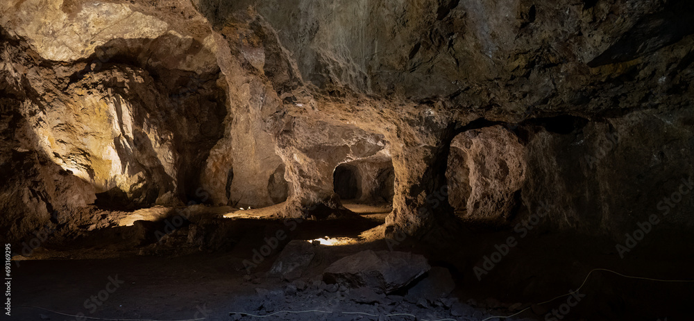 Dimly lit cave interior with rocky surfaces and shadows, creating a ...