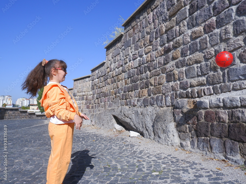 Little girl playing ball on the stone paved street.A girl playing by ...