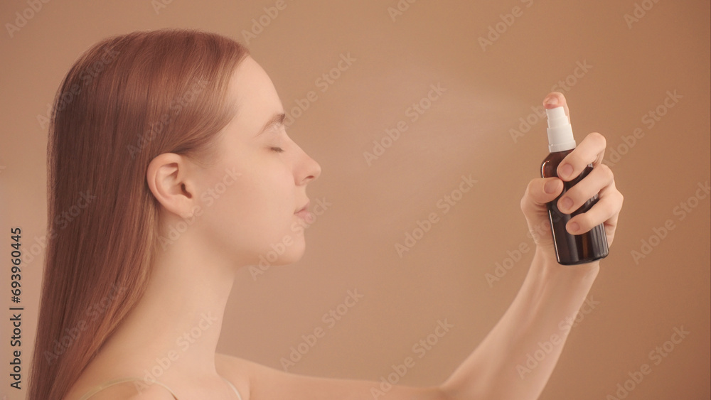 Young woman sprays a facial spray mist or thermal water, soothing tonic ...