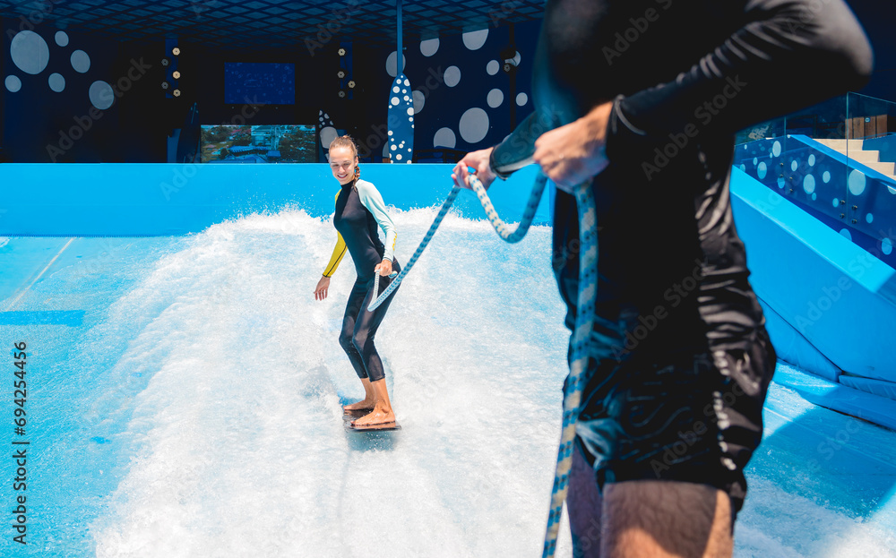 Beautiful young woman surfing with trainer on a wave simulator at a ...