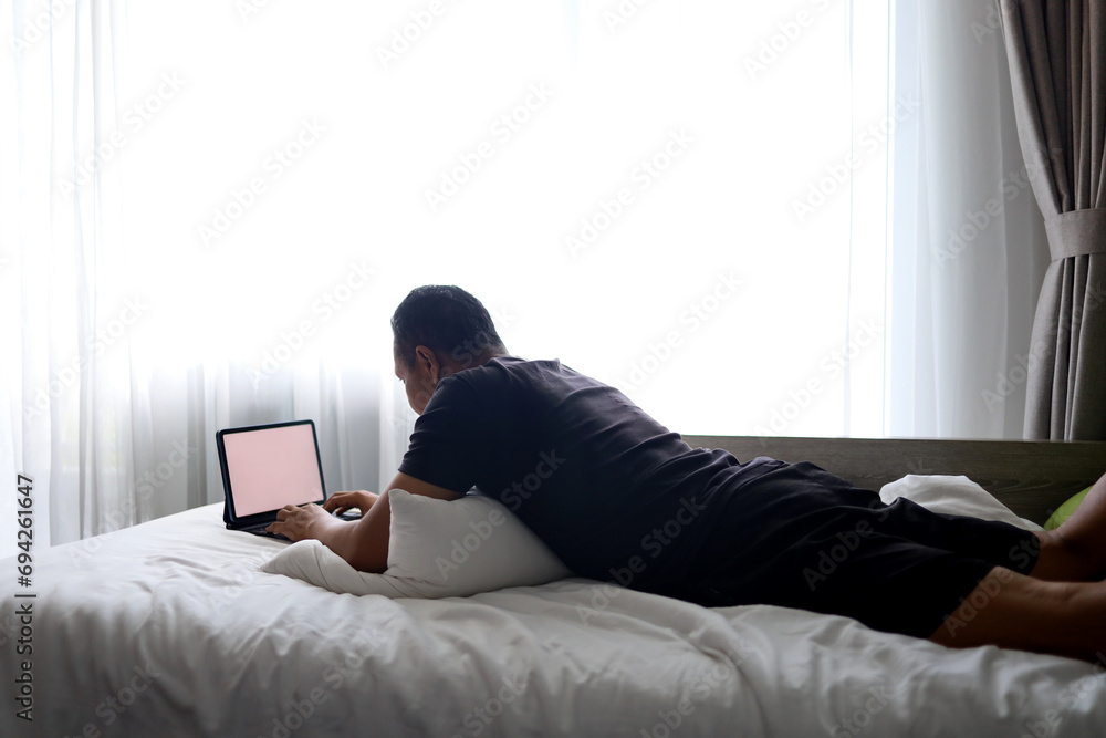 back view of man lying in bed at home, using modern pc laptop, making ...