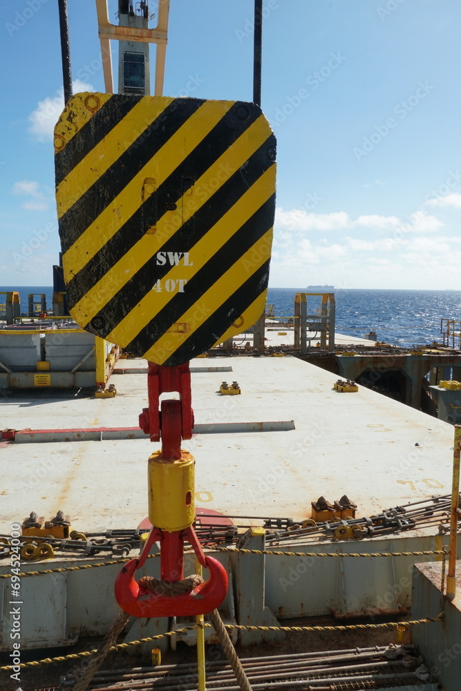 Red steel hook and black and yellow hoist block of ship's cargo crane ...