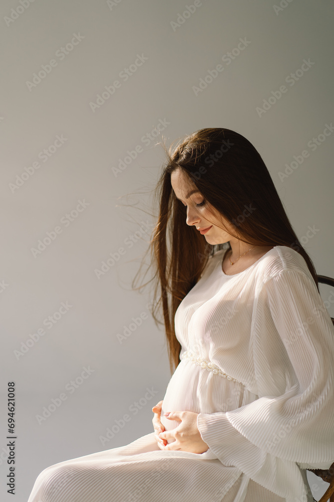 Cute young Pregnant girl sitting on the white studio in warm light with ...