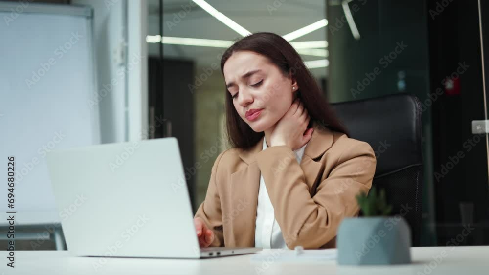 Frustrated business woman feeling pain in neck while sitting at office desk and typing on modern ...