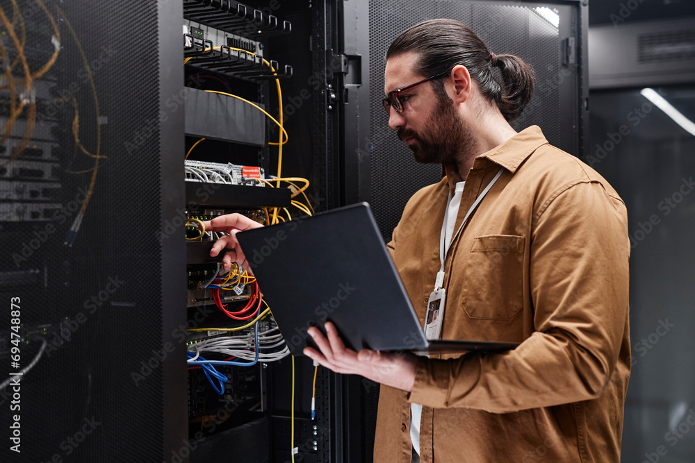 Engineer holding laptop and examining cables in server room Stock Photo ...