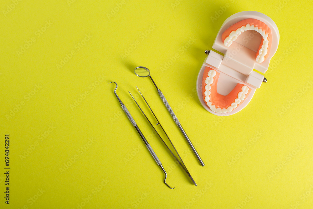 dental instrument on a yellow background near a dental jaw mockup. The ...