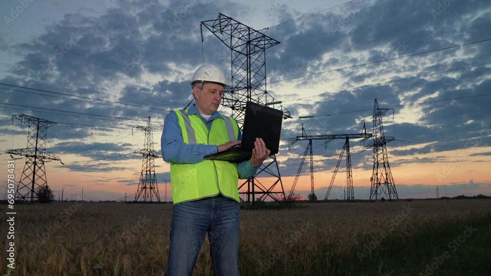 Man worker conducts examination of power transmission lines with laptop ...