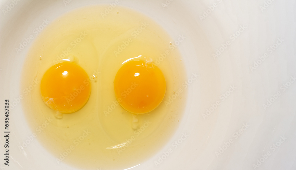 Two bright yellow raw fresh egg yolks and in white plate. Top view ...