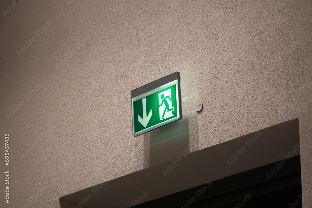Fototapeta Escape route sign above a door on a wall. The illuminated ...