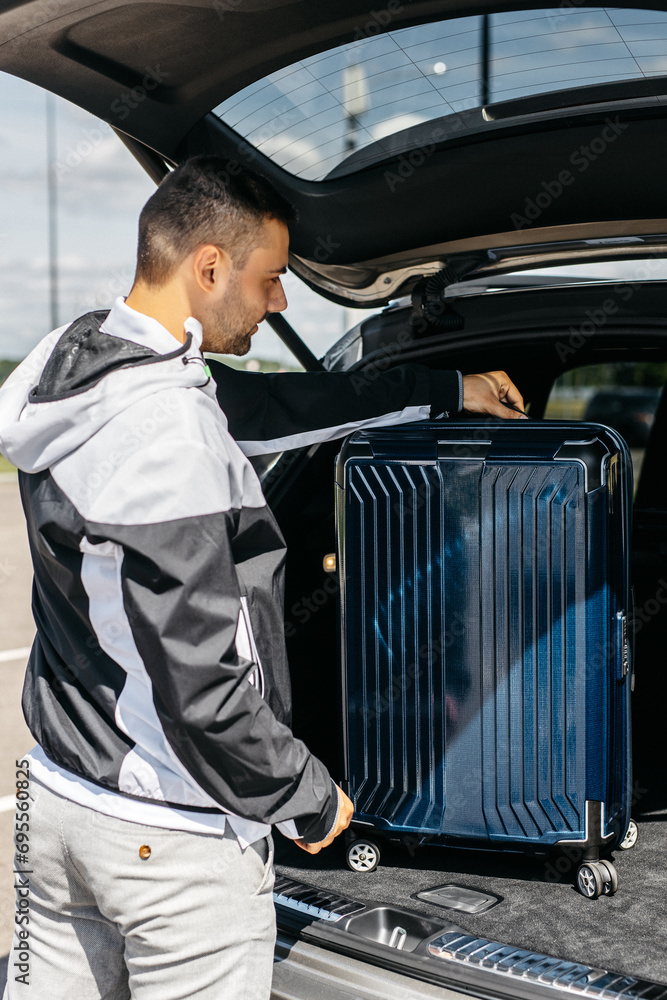 Close-cup a young man puts his suitcase in the back of the car and ...