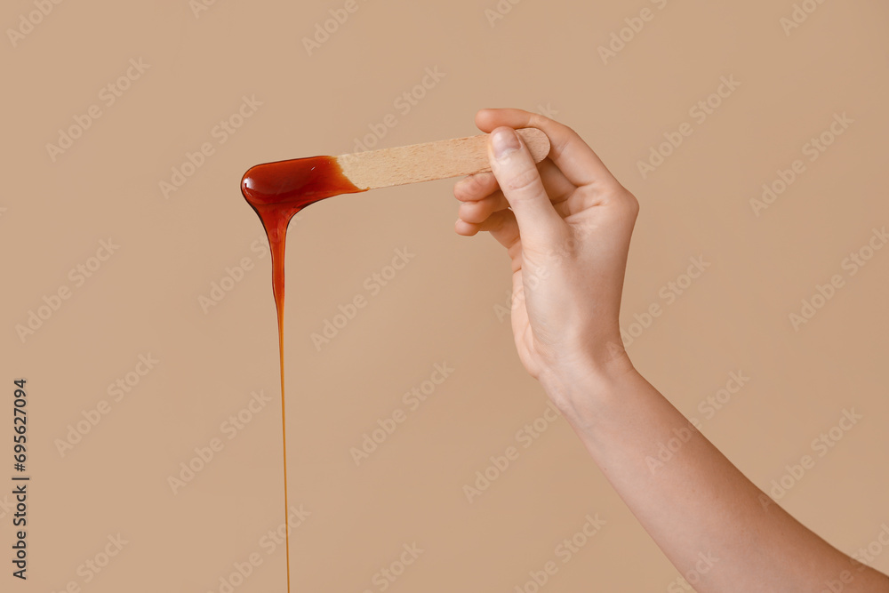 Female hand with sugaring paste for hair removal on brown background ...