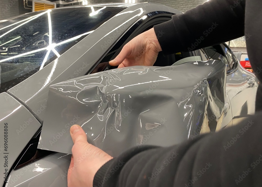 The process of wrapping vinyl film on the side mirror of a car in close ...