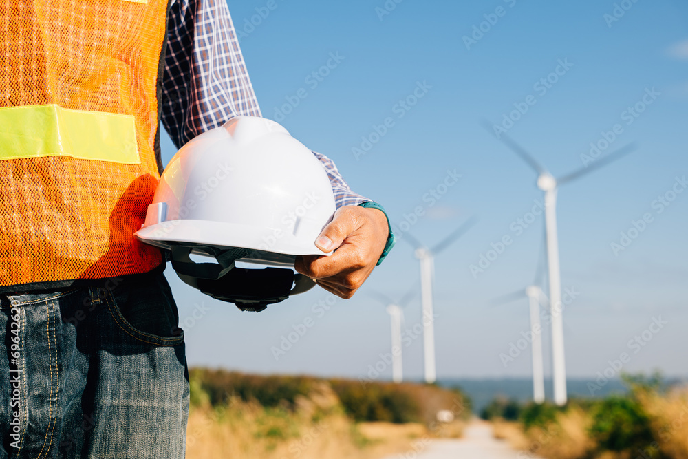 Engineer stands at wind turbine field holding safety helmet. A symbol ...