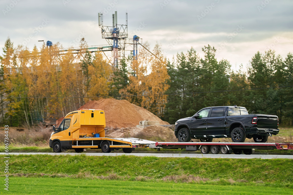 A tow truck carries a broken pick-up truck on a flatbed trailer on the ...