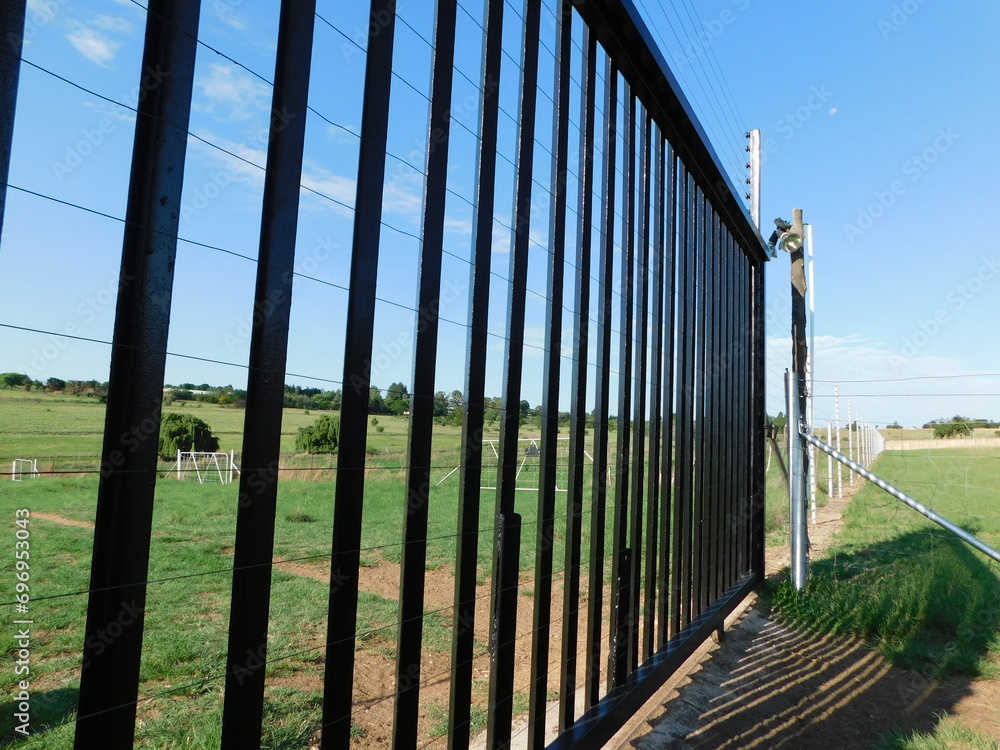 Closeup of a large black metal farm gate with electric fencing over and ...