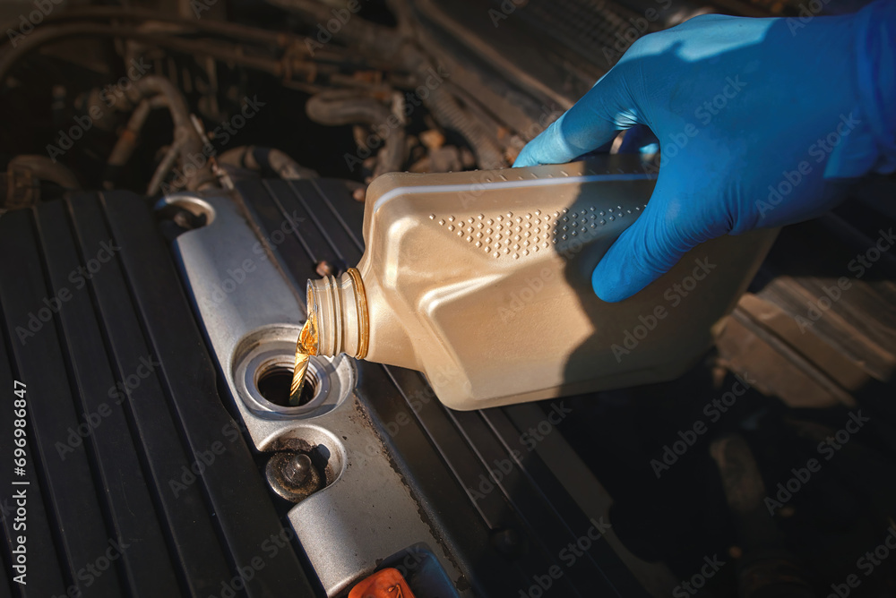 Mechanic pouring oil into the engine at car service station. Man top up ...
