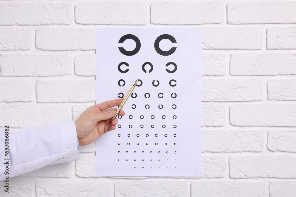 Ophthalmologist pointing at vision test chart on white brick wall ...