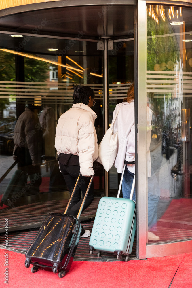 Young female tourists with wheeled luggage entering through revolving ...