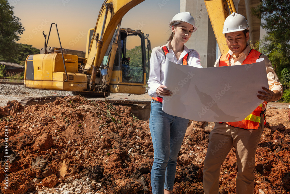 Asian male engineer and female worker wearing hard hats stand holding ...