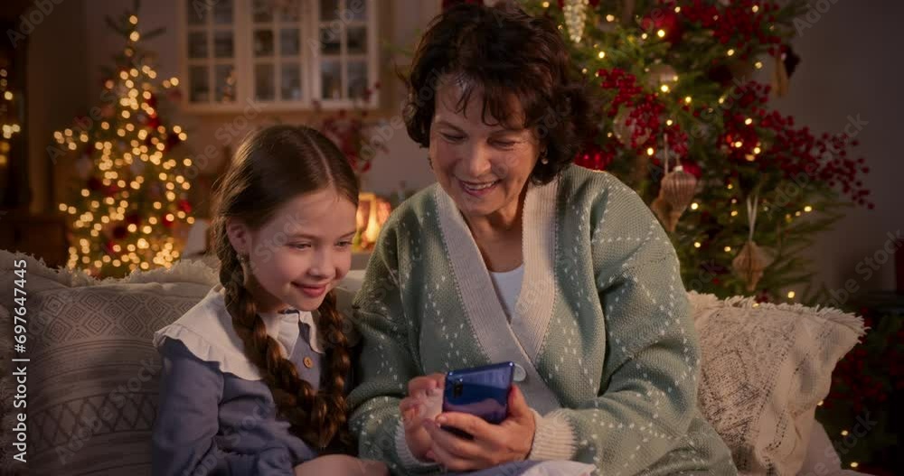 grandma and granddaughter sit on couch near christmas tree with ...