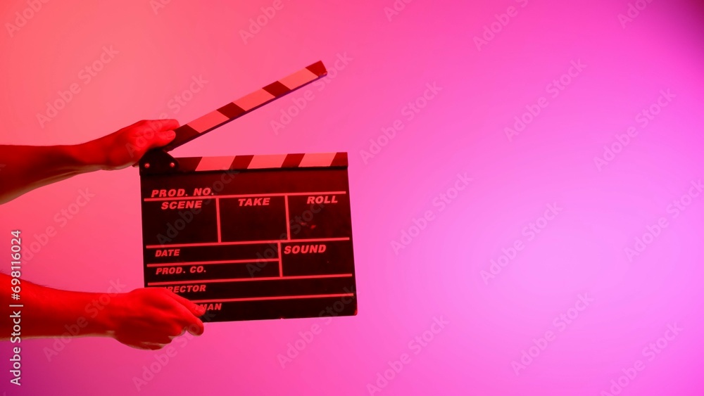 Hand is holding Black clapper board or movie slate on a pink background ...
