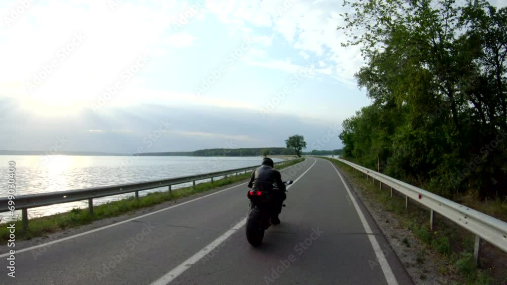 Biker riding on modern sport motorbike through road near lake ...