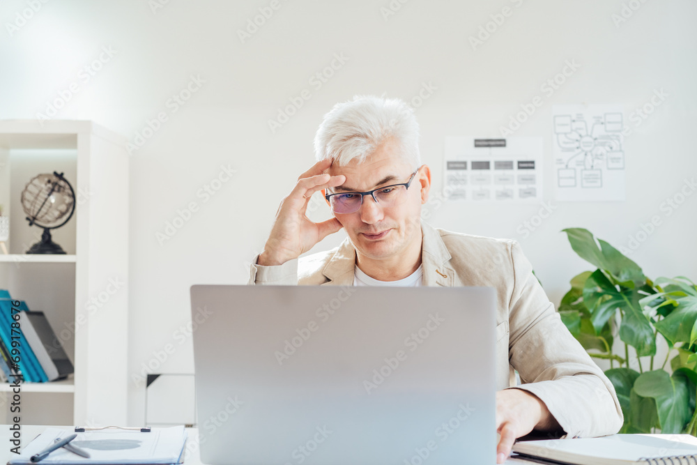 Middle aged confused business man sitting in front of laptop looking at ...