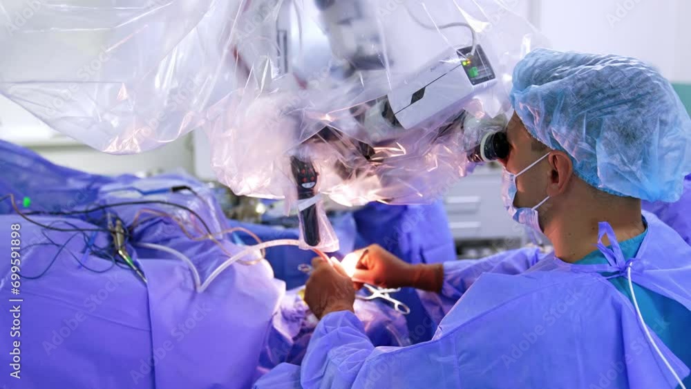 Neurosurgeon stands looking into neuro microscope using the metal tools ...