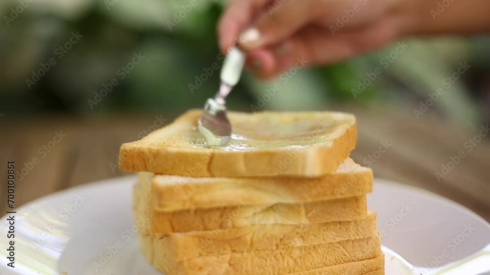 A person's hand gently spreads organic butter onto white bread. The ...