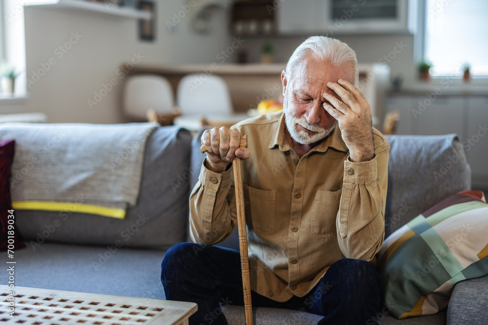 Depressed old man sitting at home while holding walking stick. Retired ...