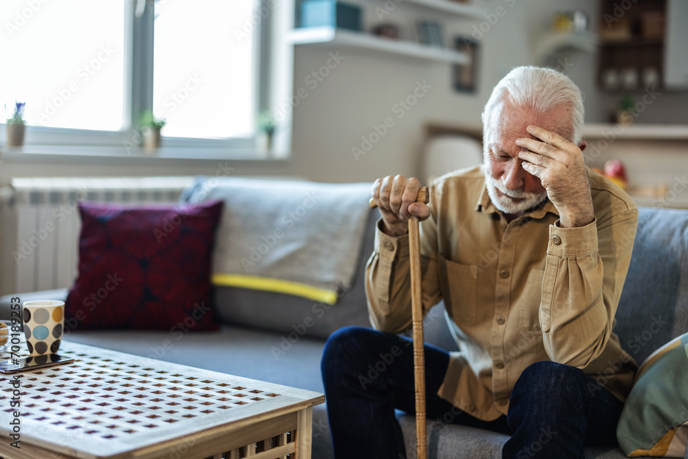 Depressed old man sitting at home while holding walking stick. Retired ...